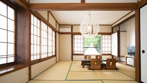 Quarto japonês tradicional com tatames, uma mesa baixa e almofadas, e um candeeiro pendente.