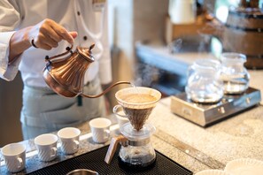 Uma estação de preparo de café com cafeteira, xícaras e uma balança.