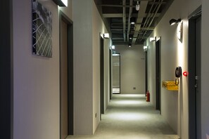 Um corredor com portas em ambos os lados, um extintor de incêndio e um telefone na parede direita.