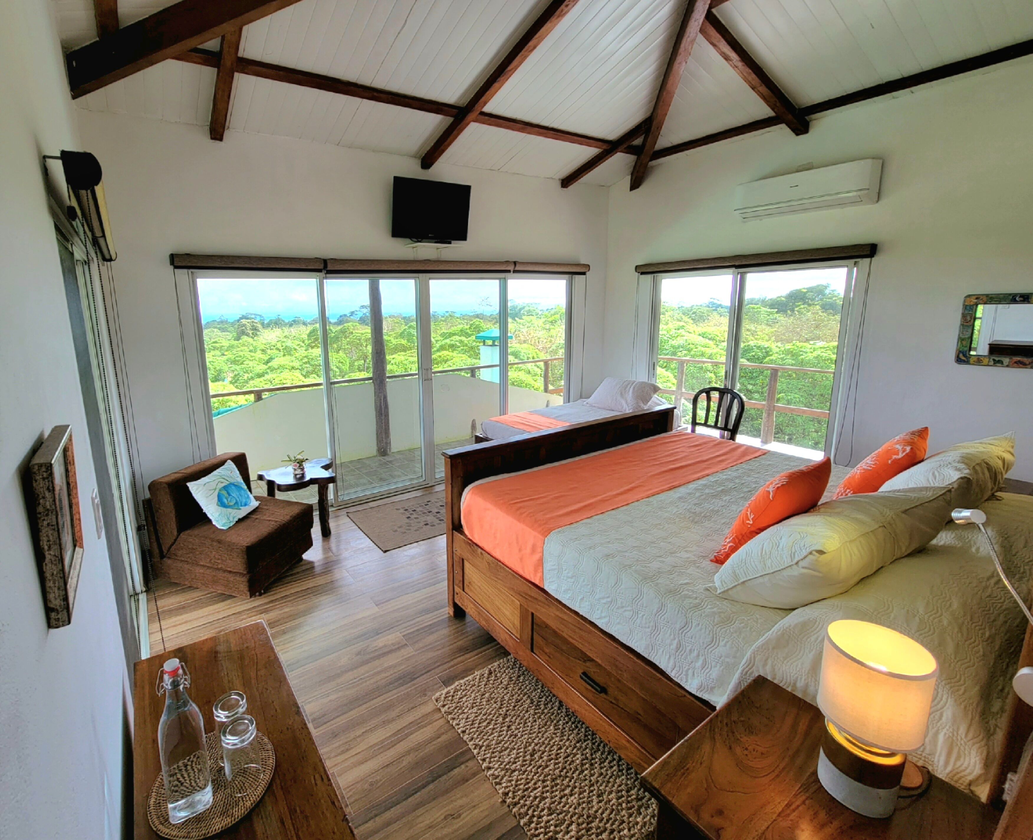 Quarto com cama grande, mesa de cabeceira com abajur, cadeira e vista para o exterior.