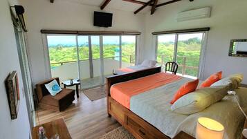 Quarto com cama grande, mesa de cabeceira com abajur, cadeira e vista para o exterior.