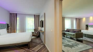 Quarto de hotel com cama, escrivaninha, poltrona, sofá e televisão.