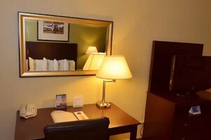Quarto de hotel com uma cama, uma escrivaninha com luminária, telefone e televisão.