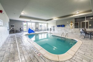 Uma piscina interior com chão em mosaico, posto de salva-vidas e área de estar com mesas e cadeiras.