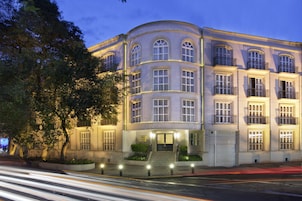Um edifício de vários andares com fachada curva, grandes janelas e entrada central com degraus.