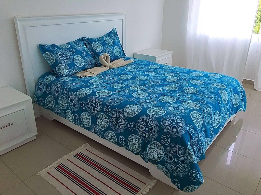 Quarto com cama, mesas de cabeceira e tapete listrado.