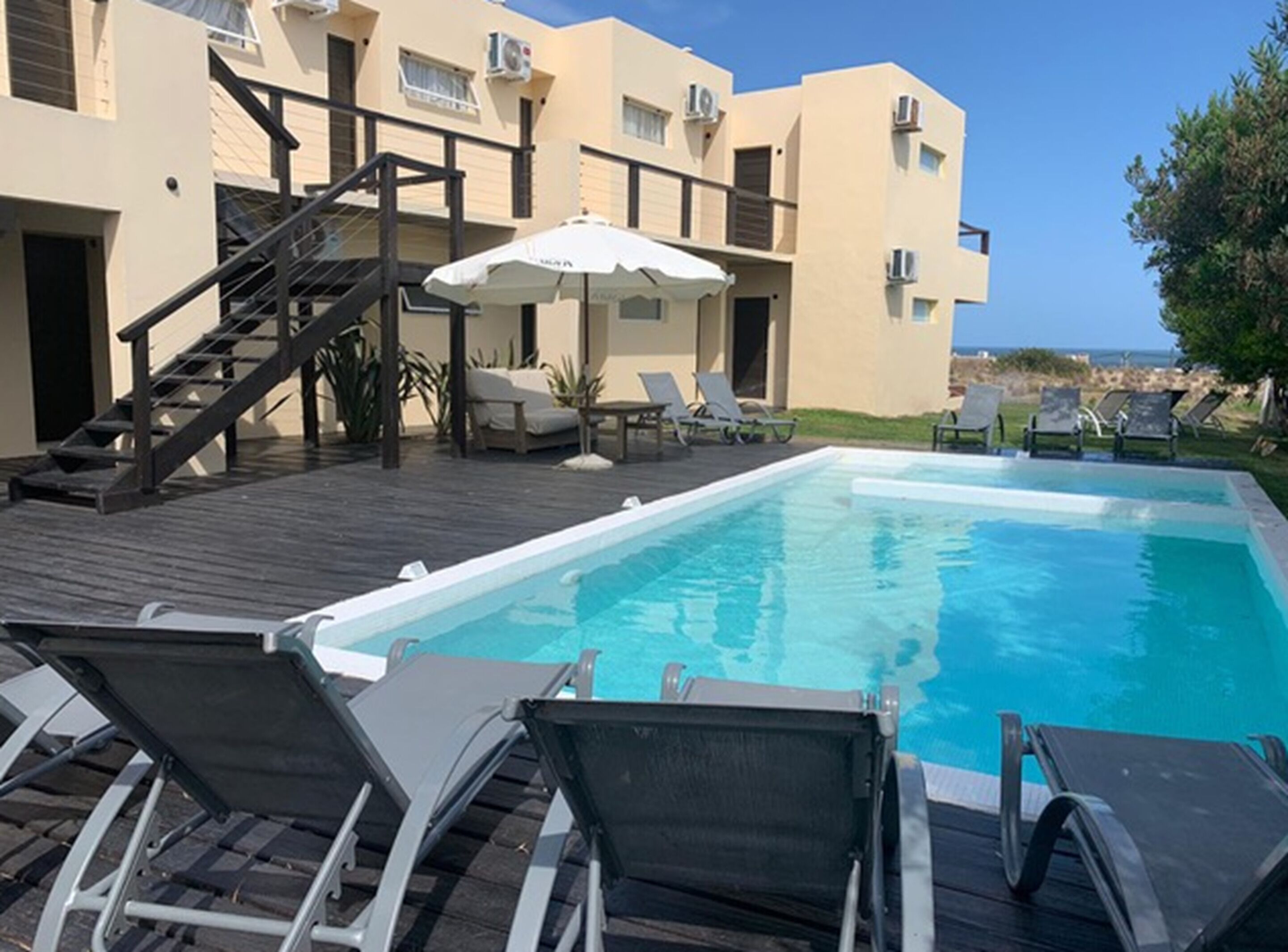 Piscina com espreguiçadeiras, escadaria e um edifício com varandas.