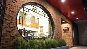 Edifício de tijolos com uma grande janela circular que mostra o interior de um restaurante, uma parede de tijolos e um toldo vermelho.
