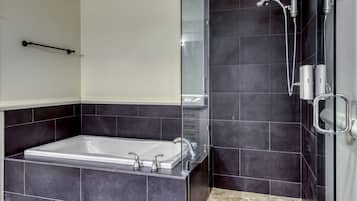 Um banheiro moderno com uma banheira livre, um chuveiro com proteção de vidro e paredes com azulejos escuros.