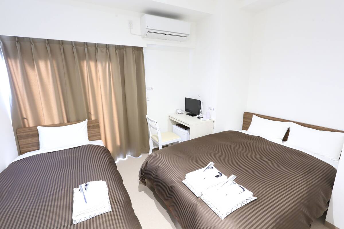 Quarto de hotel com duas camas, uma escrivaninha, uma cadeira e um ar condicionado.