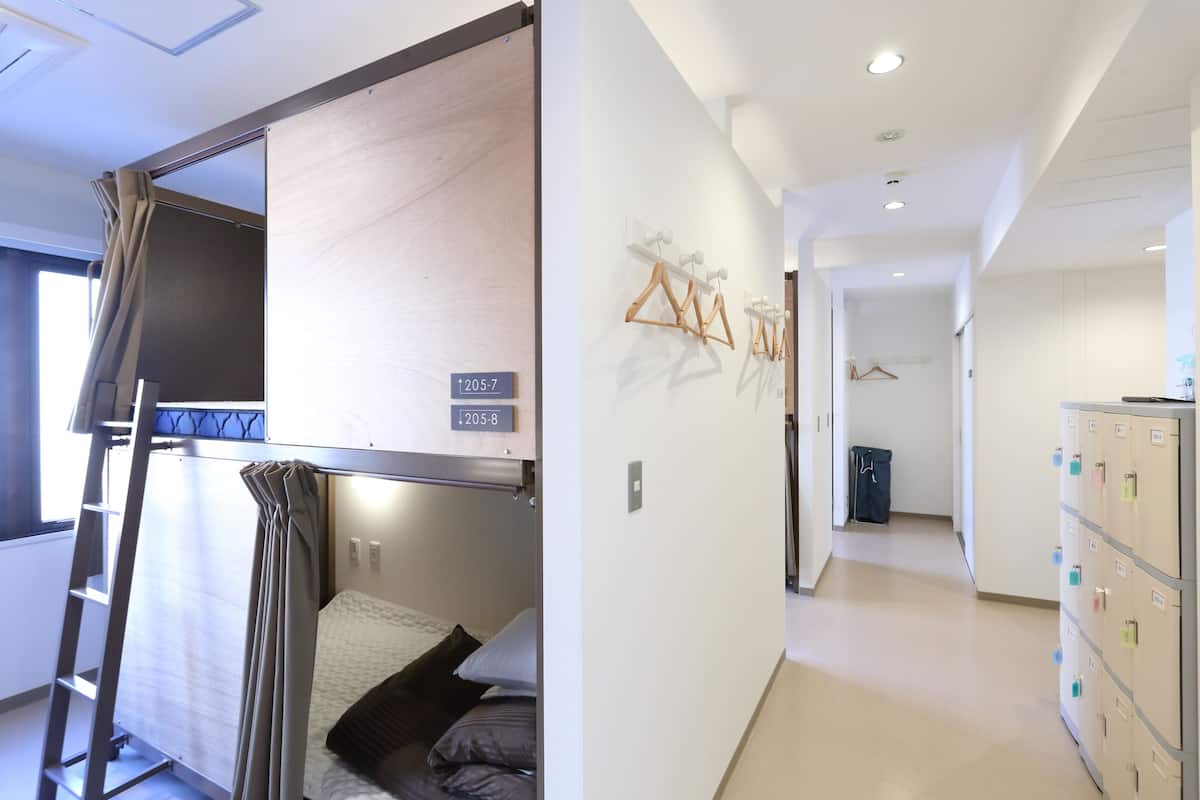 Quarto com beliche, escada e cortina. Há um corredor com armários e porta-casacos.