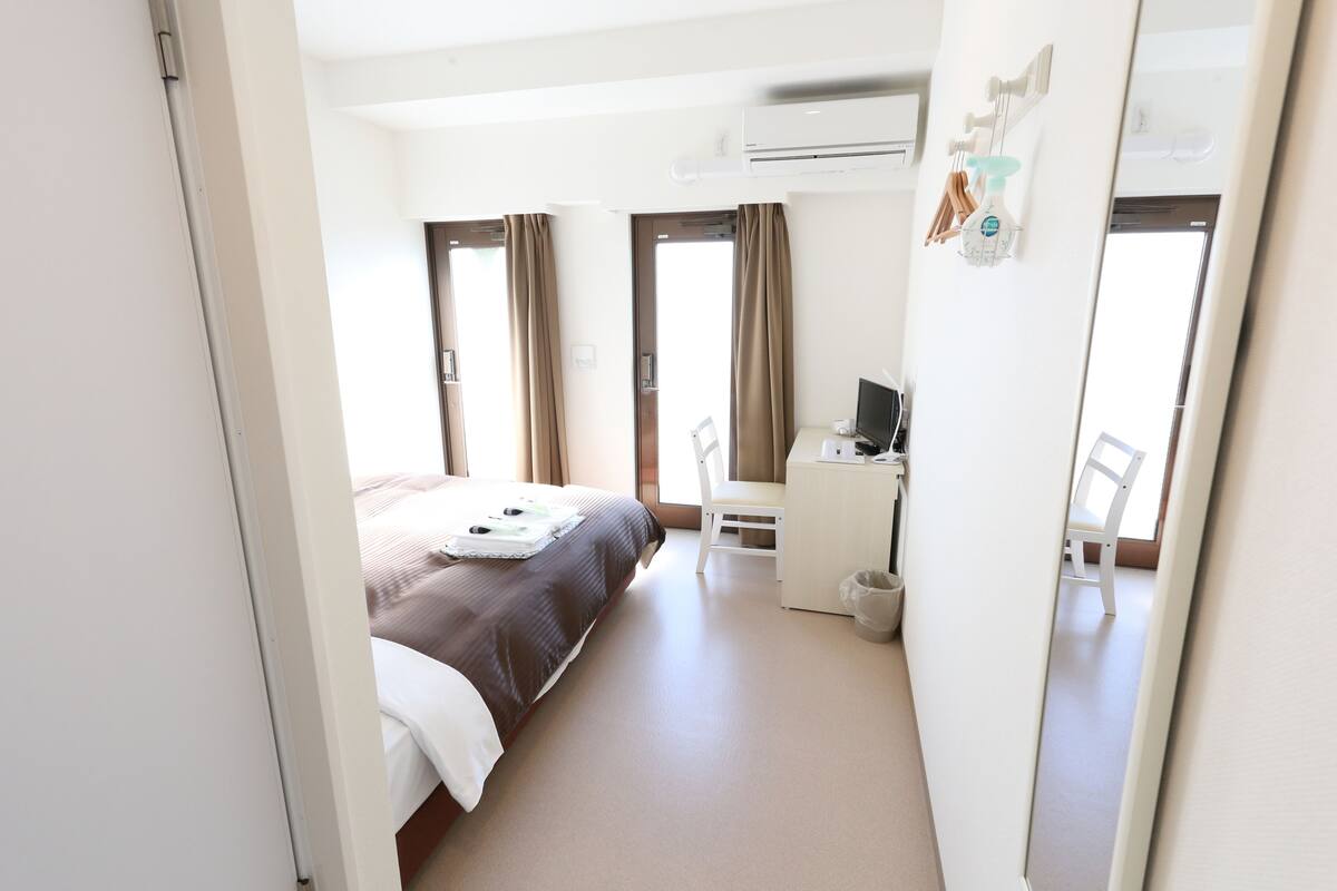 Quarto de hotel com cama, escrivaninha, cadeira e ar condicionado.