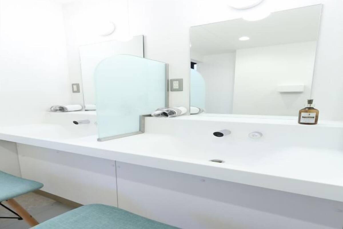 Casa de banho com duas pias, um espelho e um frasco de gel desinfetante.