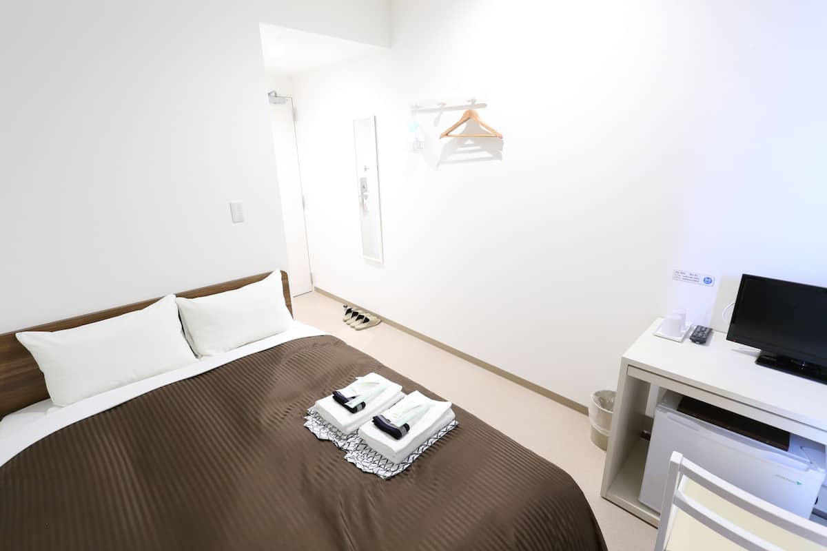 Quarto de hotel com cama, escrivaninha e computador, além de televisão.