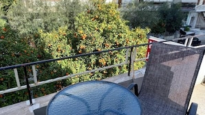 Uma varanda com uma mesa de vidro redonda e uma cadeira de tela, com vista para um jardim de laranjeiras.