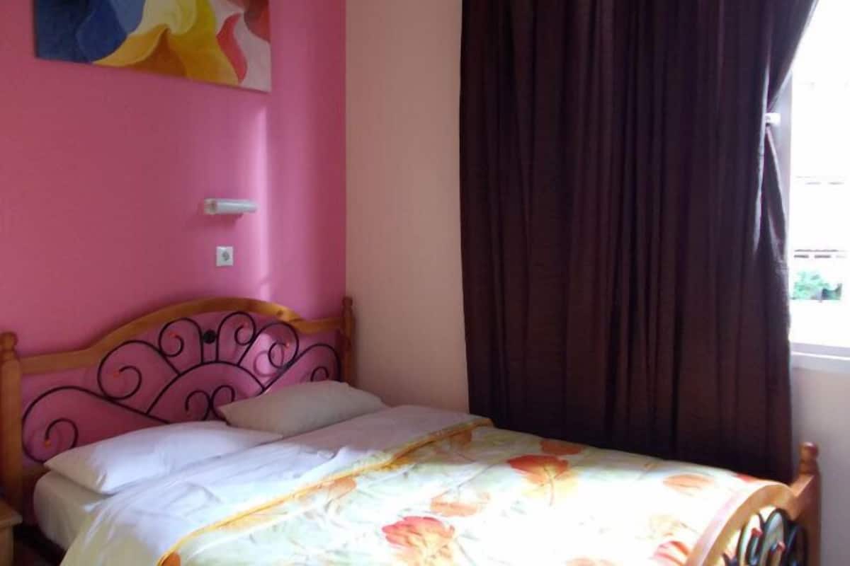 Um quarto com uma cama, parede rosa, um quadro e uma janela com cortinas.
