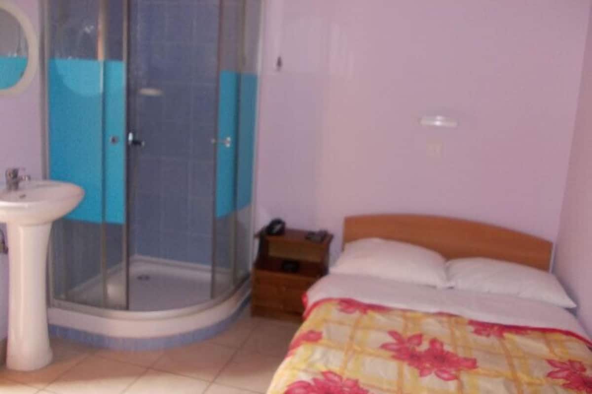 Quarto com cama, mesa de cabeceira, cabine de duche e lavatório.