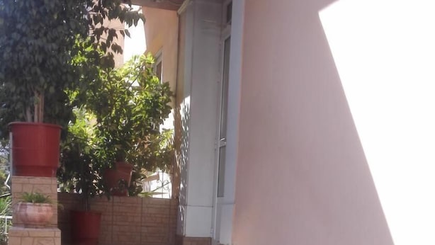 Degraus de pedra levam a uma porta, com plantas em vasos à esquerda e um muro de azulejos à direita.