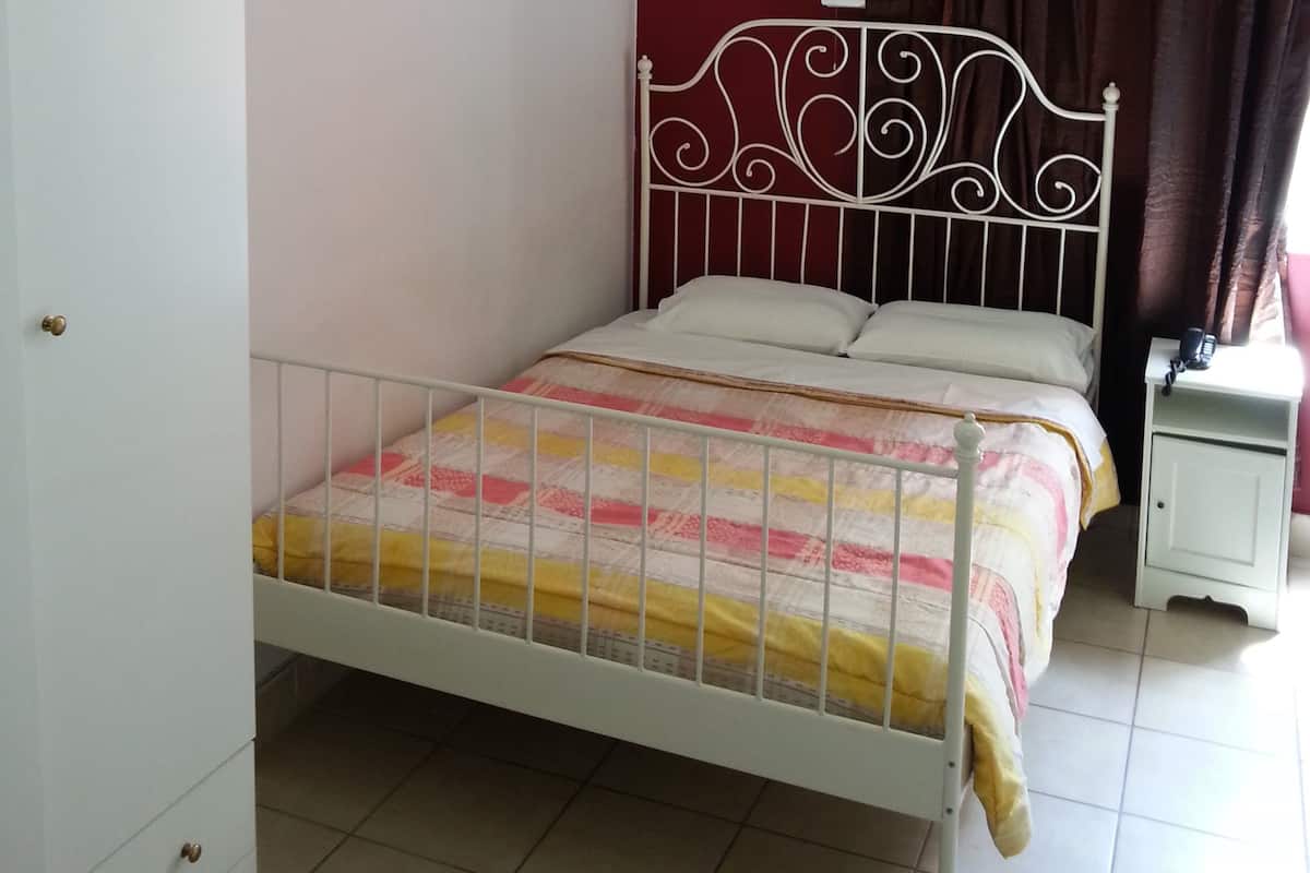 Quarto de casal com uma cama de solteiro, cabeceira de metal, mesa de cabeceira e parede vermelha.
