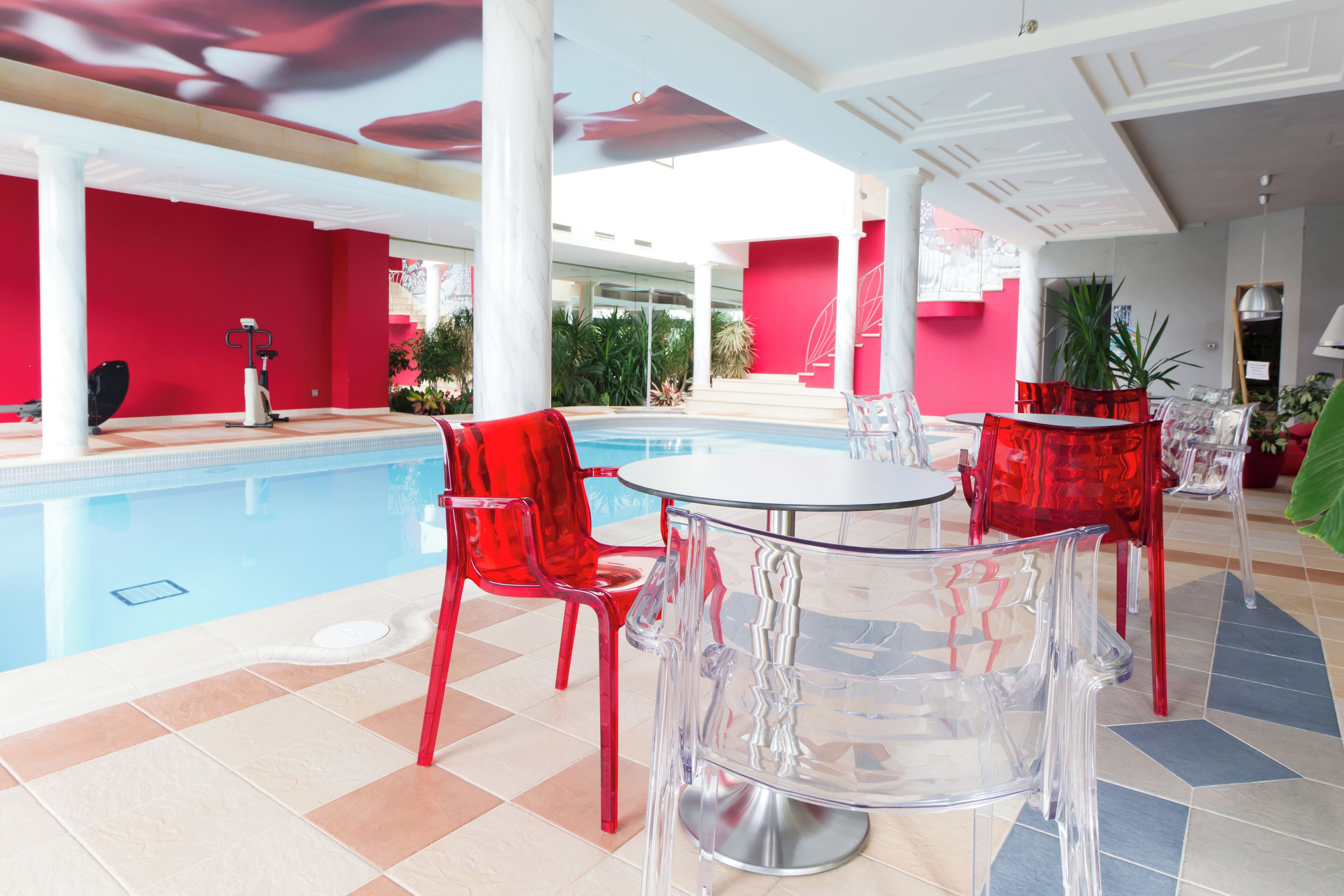 Uma área de piscina com cadeiras vermelhas e uma mesa de vidro, emoldurada por uma decoração em vermelho e branco.