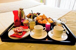 Bandeja de café da manhã com croissants, frutas, geleia e café sobre a cama.