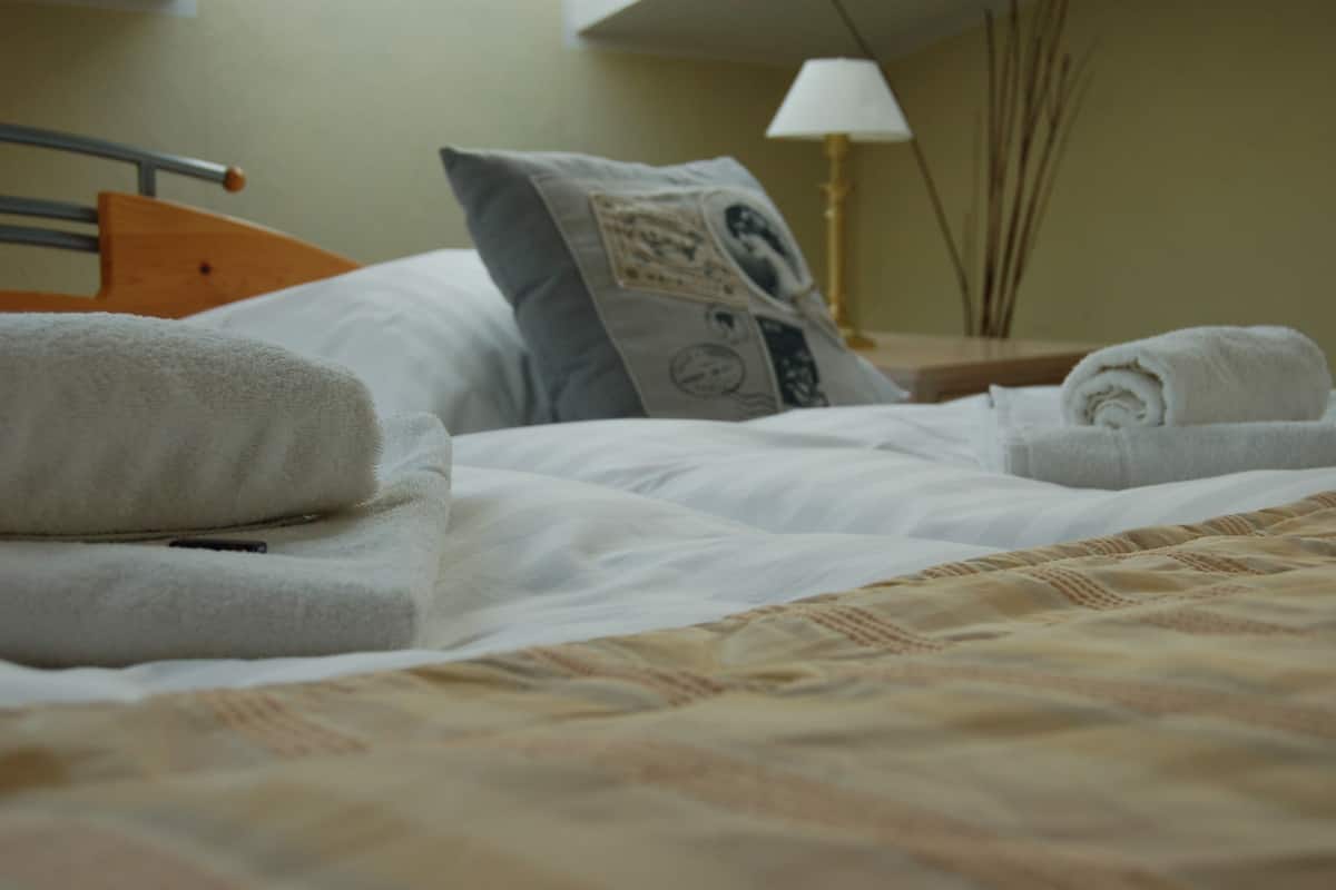 Uma cama bem arrumada com um edredom estampado, um travesseiro com um aplique e uma toalha enrolada ao lado.