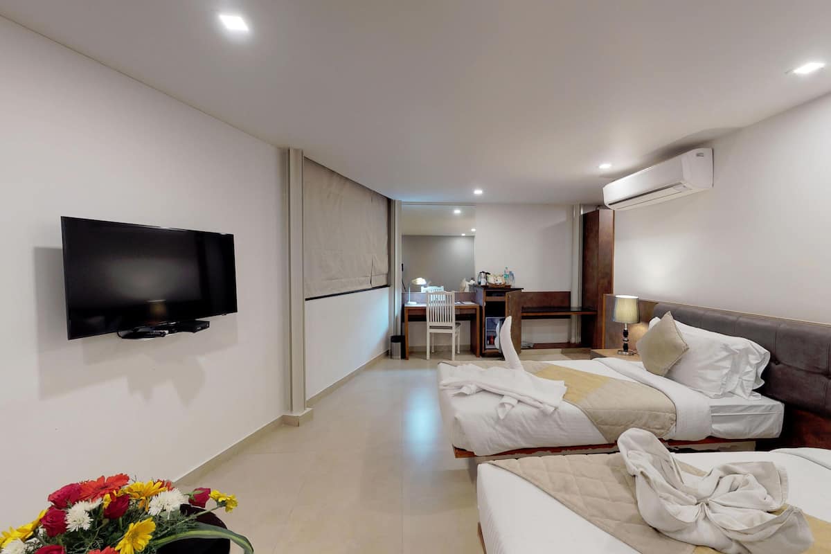 Quarto de hotel com televisão de tela plana na parede, cama com roupa branca, sofá de couro marrom e escrivaninha com cadeira.