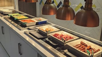 Buffet com diversos alimentos e luminárias pendentes de cobre.