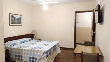 Quarto com cama, mesa, cadeira, abajur, televisão e porta.