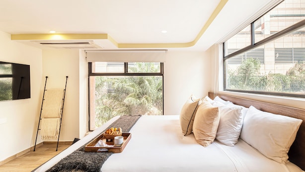Quarto moderno com uma cama grande, vista para o verde lá fora e uma bandeja com itens de café da manhã.