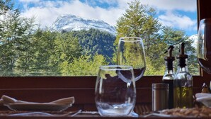 Uma mesa com copos de vinho e garrafas, um saleiro e um prato, vista para a montanha pela janela.