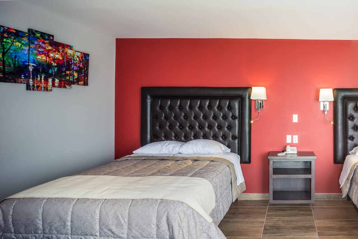 Quarto de hotel com duas camas, paredes vermelhas e uma mesinha de cabeceira com abajur.