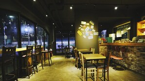 Um restaurante com mesas, cadeiras, um espaço de bar e uma parede com vários avisos e cartazes.