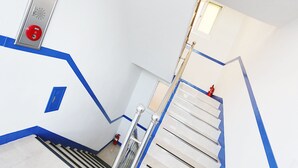 Uma escadaria moderna com detalhes em azul, um painel de alarme de incêndio e um extintor.