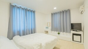 Quarto de hotel com duas camas, televisão, pequena escrivaninha e uma planta.