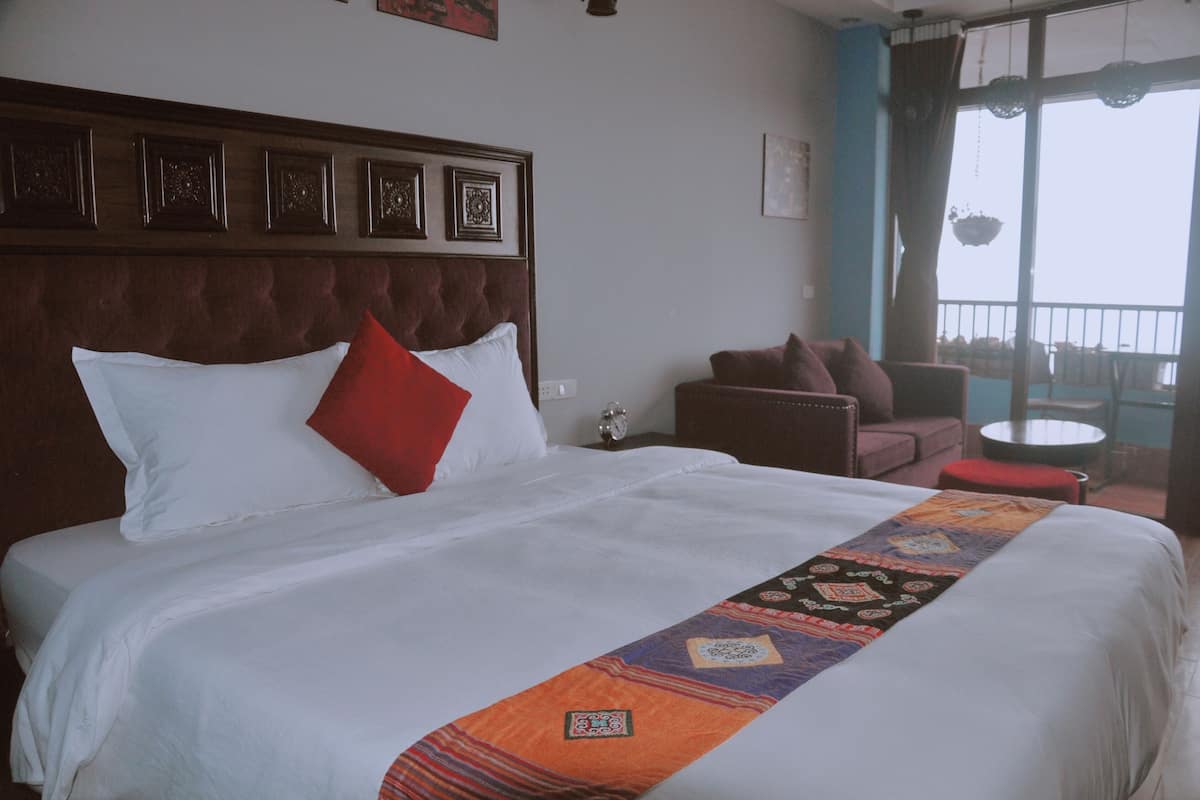 Quarto de hotel com uma cama grande, cabeceira com quadros emoldurados, varanda com vista e uma pequena mesa.