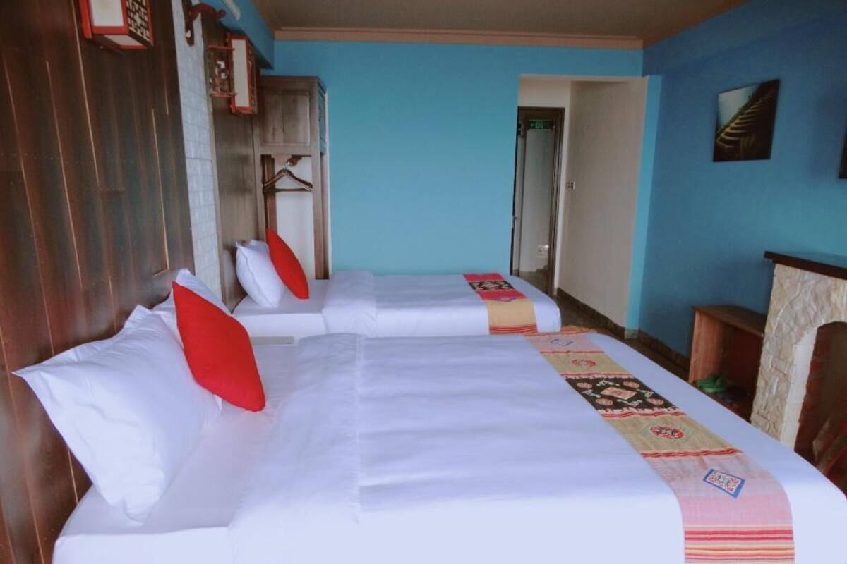 Quarto de hotel com três camas, paredes de madeira e uma parede azul de destaque.