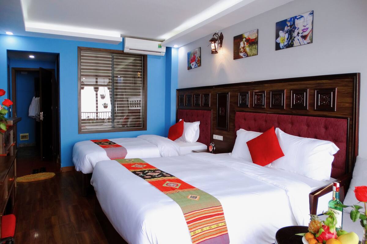 Quarto de hotel com duas camas, uma cabeceira de madeira, uma janela com persianas e uma parede com obras de arte.