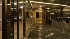 Um hall de hotel moderno com piso de mármore refletivo, painéis decorativos nas paredes e um balcão de recepção.
