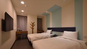 Quarto de hotel com duas camas, uma escrivaninha, uma cadeira, uma televisão e um cabideiro.