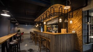 Uma área de bar com balcão de madeira, banquetas e luminárias pendentes.