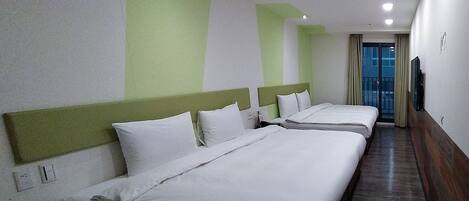 Quarto de hotel com três camas de solteiro, piso de madeira, uma parede de destaque verde e uma porta que dá para uma varanda.
