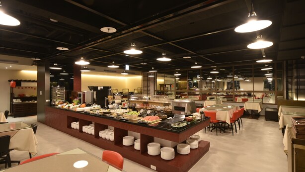 Uma área de buffet com um ponto central de serviço, várias mesas e cadeiras.
