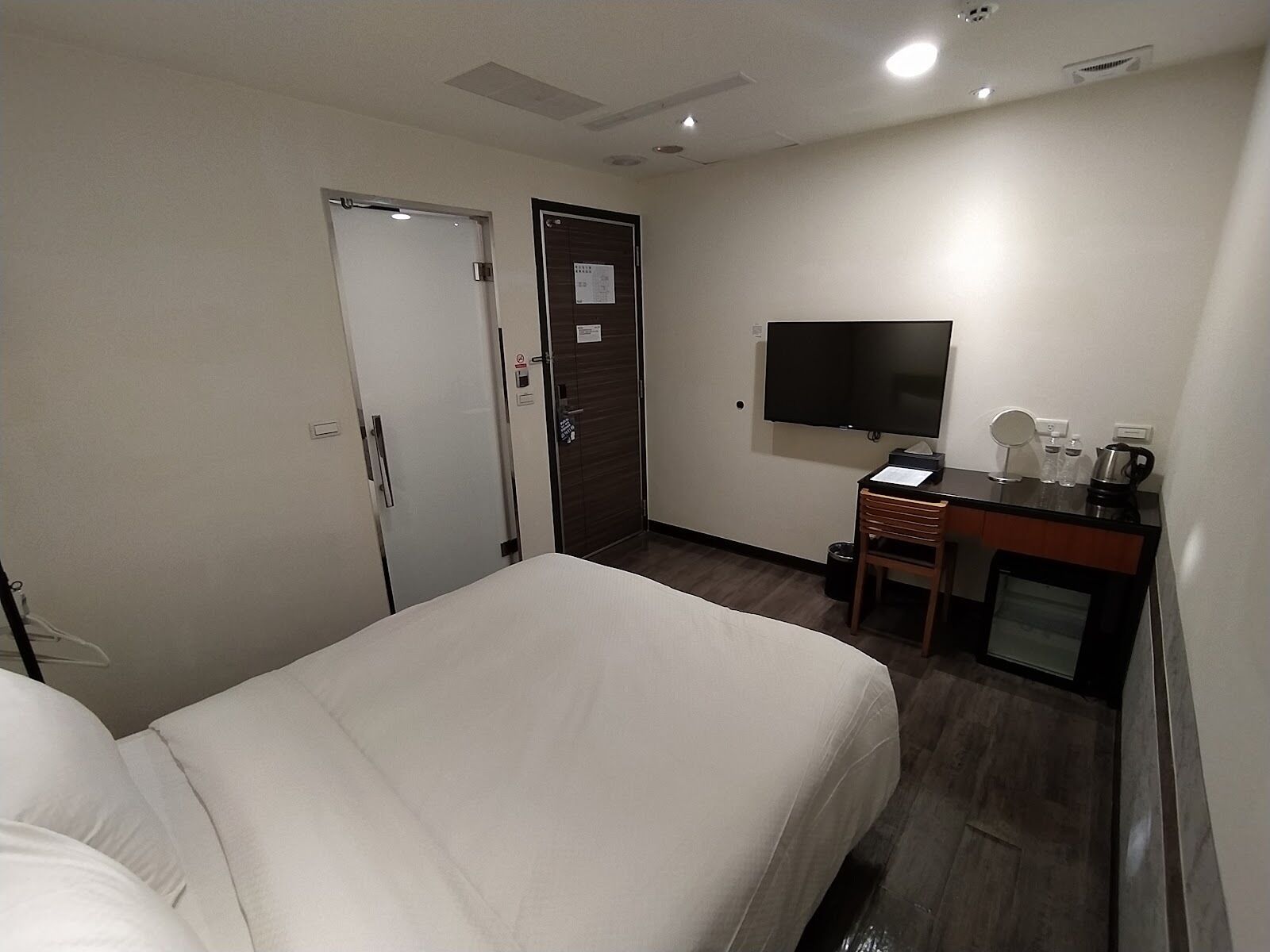 Quarto de hotel com cama, escrivaninha, computador, televisão e um pequeno espaço de estar.