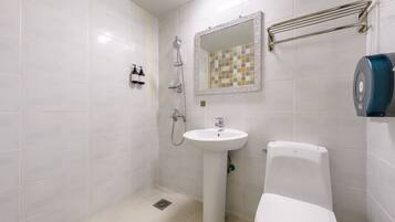 Casa de banho com azulejos brancos, lavatório suspenso, sanita, chuveiro com chuveiro de mão e barra de toalhas.