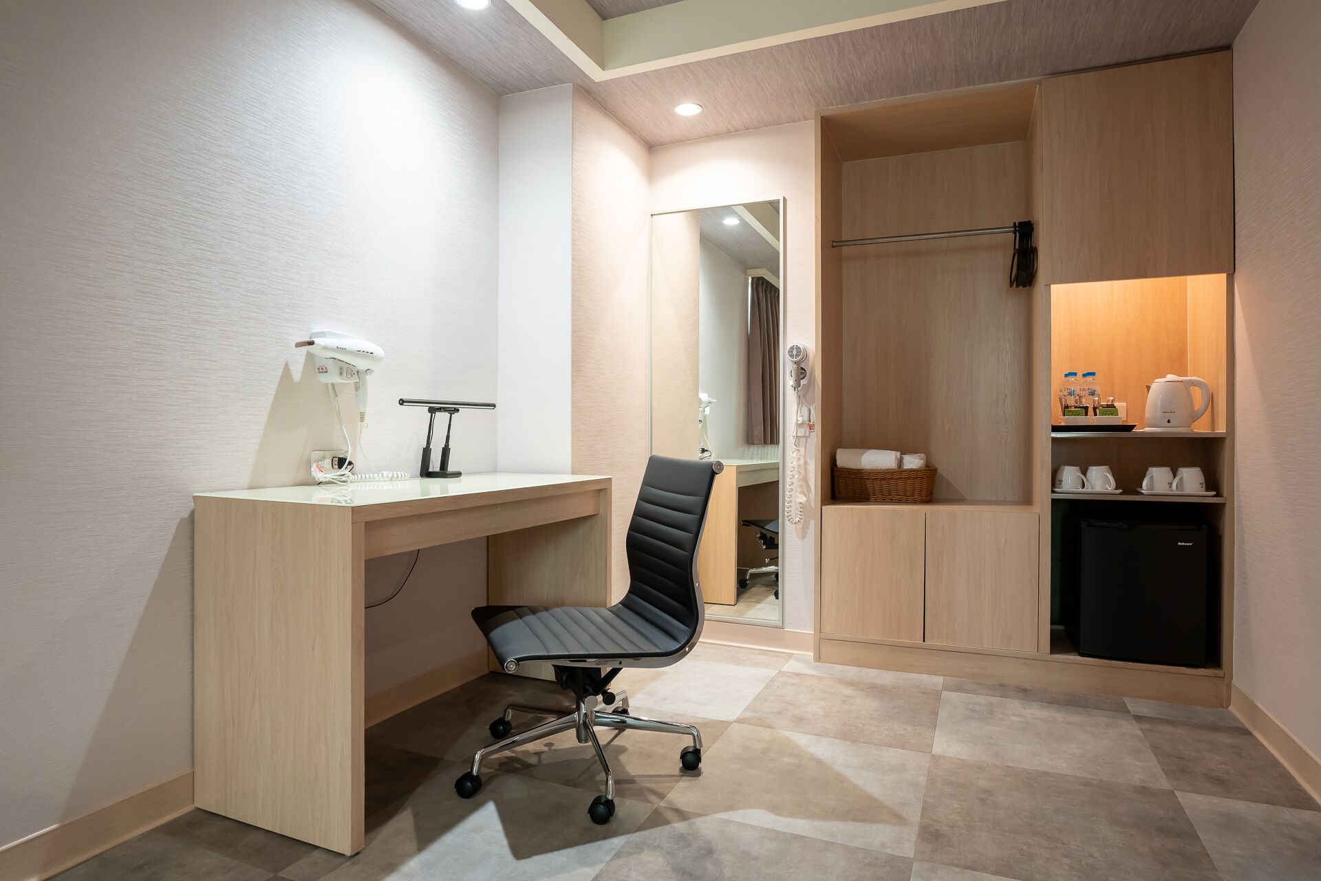 Quarto de hotel compacto com secretária de madeira, cadeira de escritório preta, pequena cozinha e closet espaçoso.
