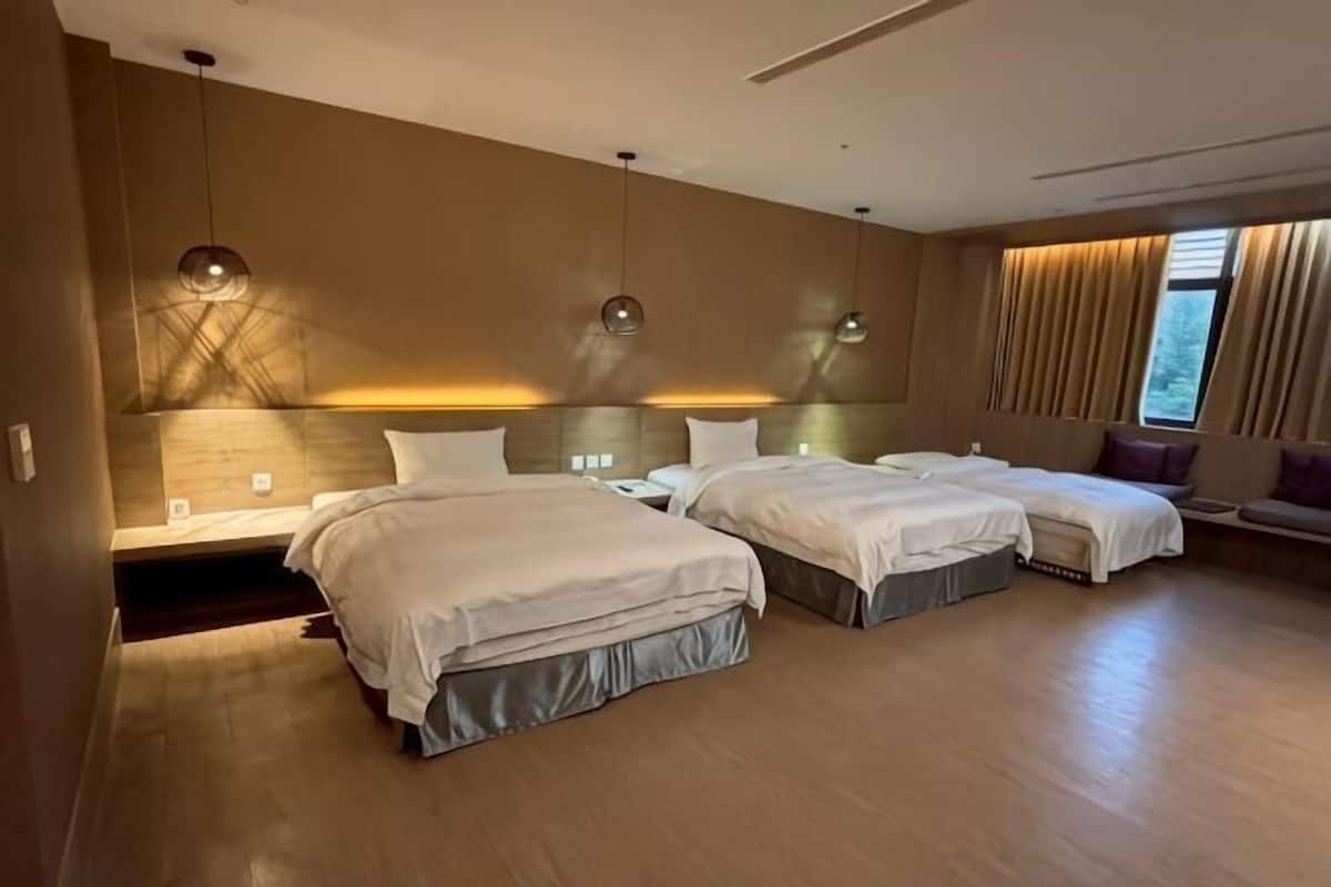 Quarto de hotel com duas camas, uma escrivaninha e uma janela com cortinas.