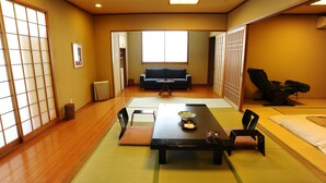 Um quarto japonês tradicional com tatames, uma mesa baixa com almofadas, um sofá e uma porta deslizante.
