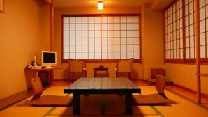 Um quarto japonês tradicional com tatames, uma mesa baixa, duas cadeiras, uma televisão e um painel shoji.
