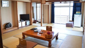 Um quarto japonês tradicional com tatames, uma mesa de madeira com almofadas, uma televisão e um frigorífico.